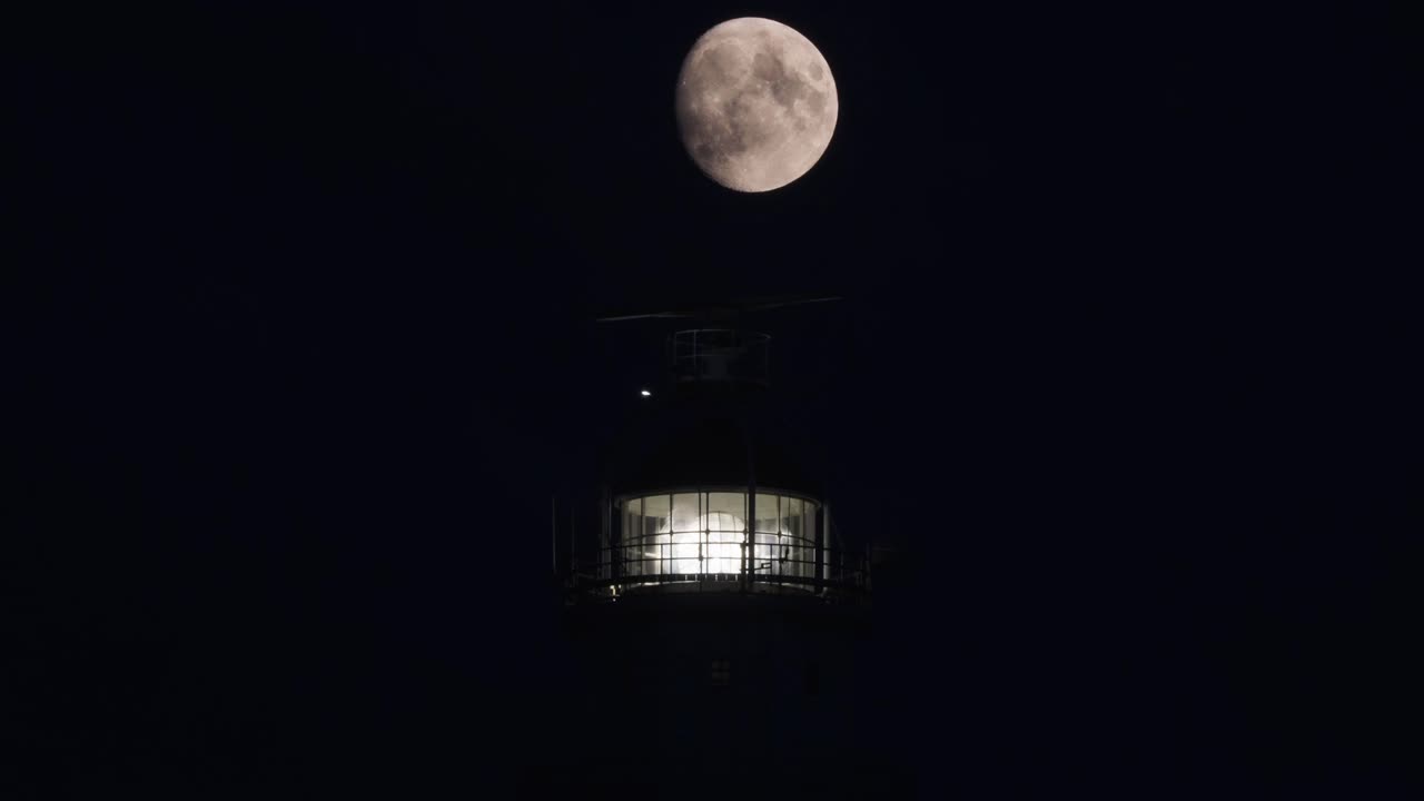 Spinning Lighthouse Beacon At Night With Full Moon Above Lighthouse At ...