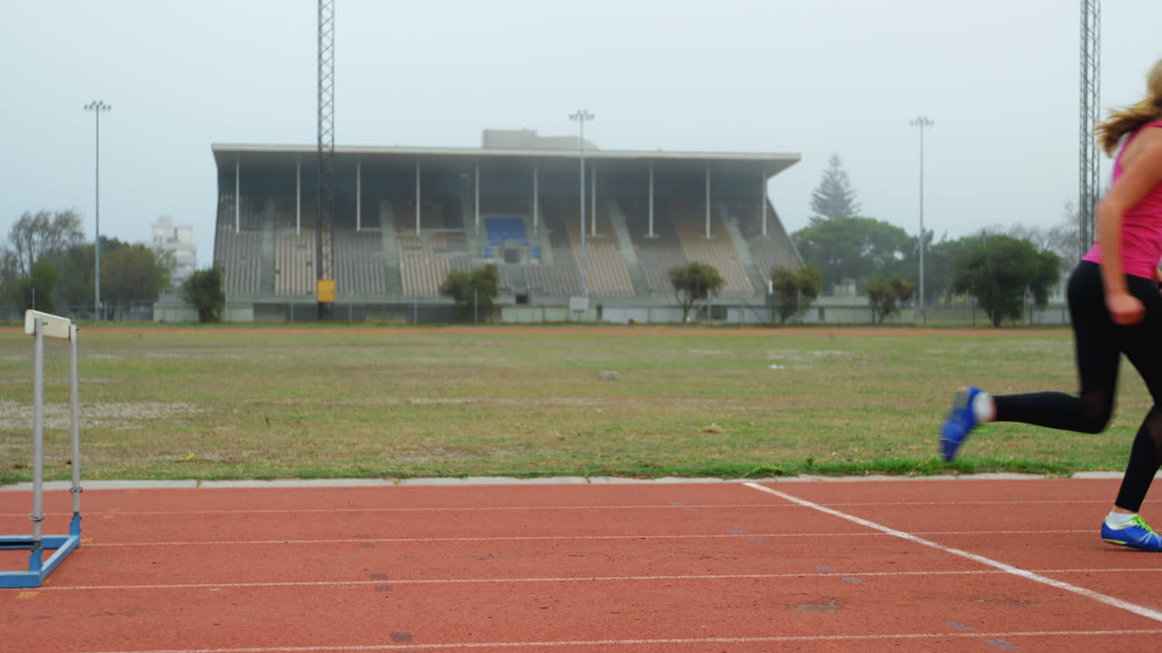 side view of caucasian female athlete jumping over hurdles on a running ...