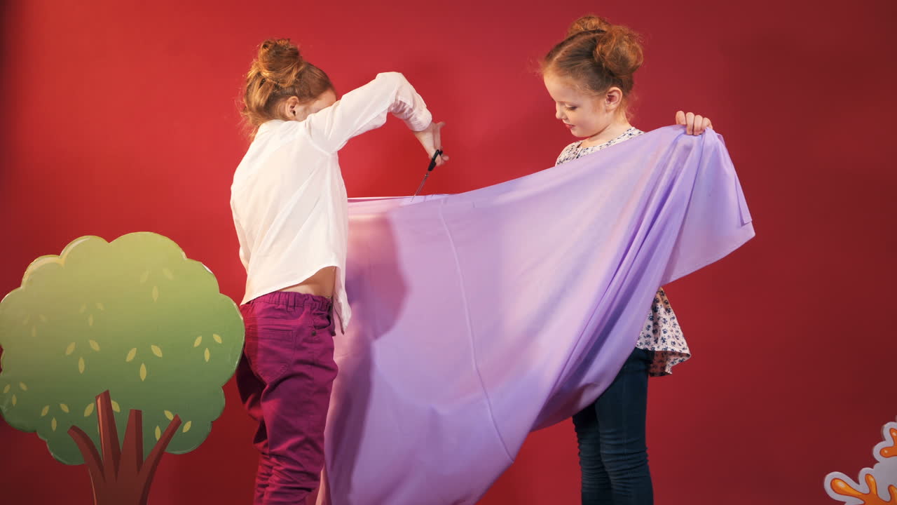 Girls cuts a piece of cloth with scissors. Studio shooting of children ...