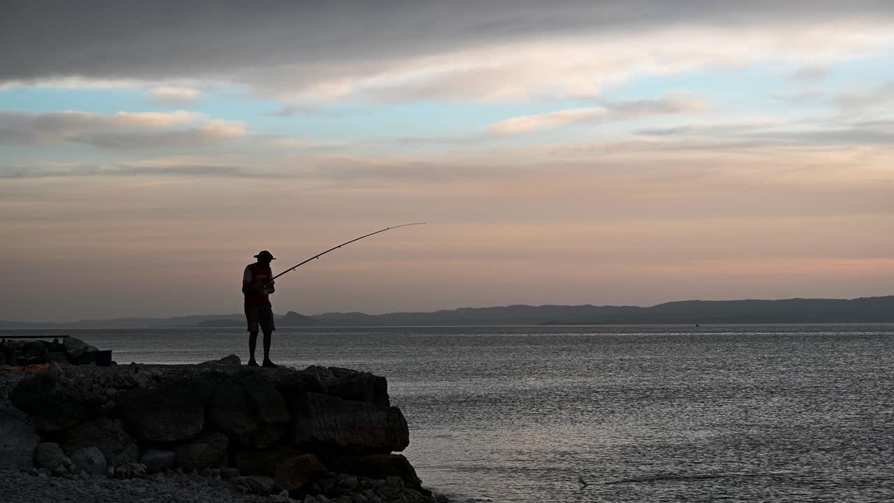 Premium stock video - Old man catching a fish from a rocky pier during ...