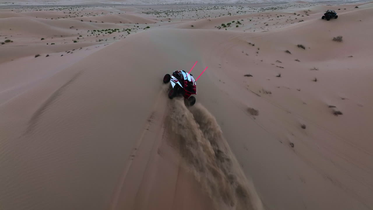 Fpv drone shot following a atv quad riding on over dunes of the dubai ...