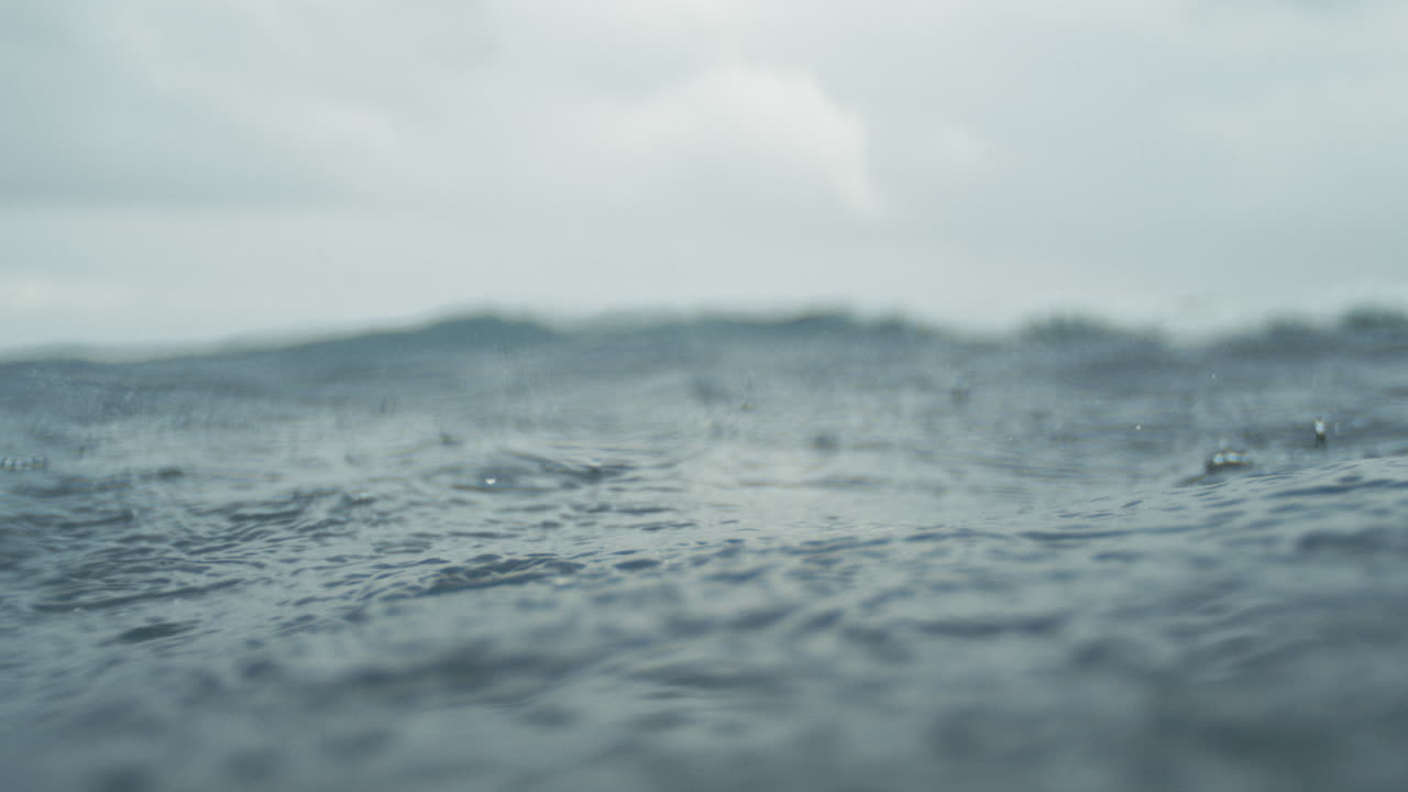 Raindrops create ripples across open water surface in super slow motion ...