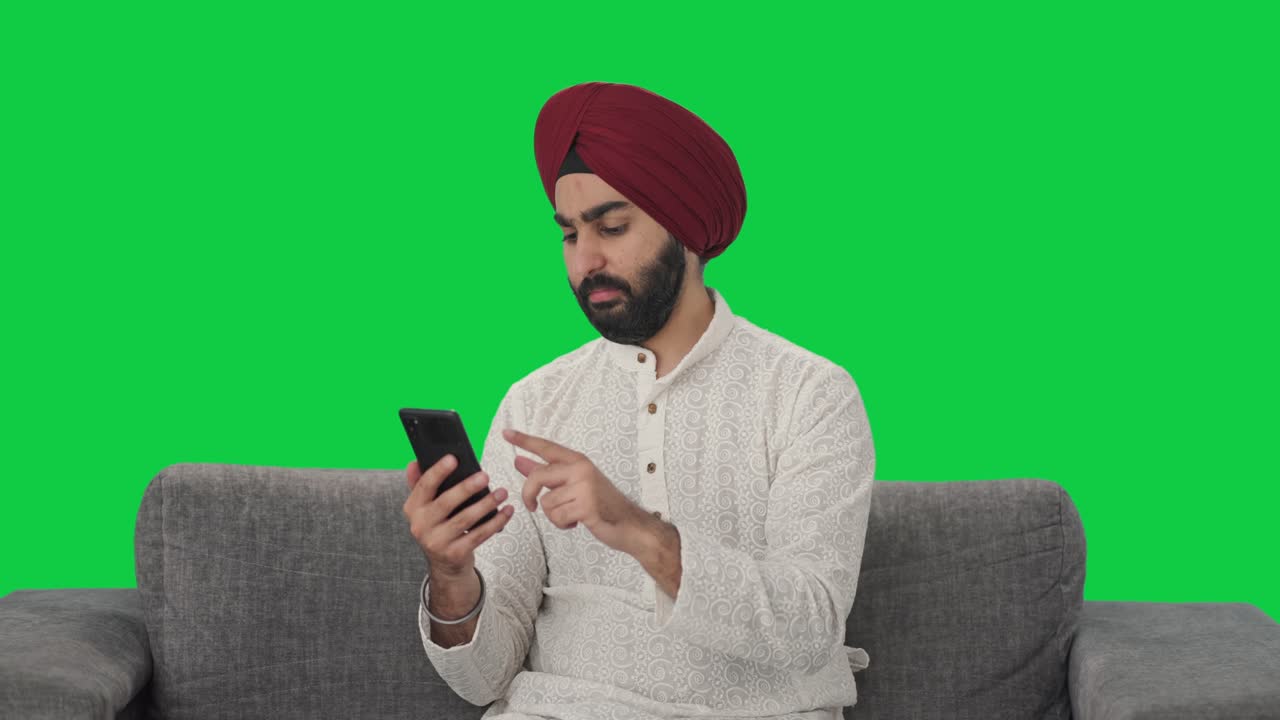 Premium stock video - Sikh indian man scrolling phone green screen
