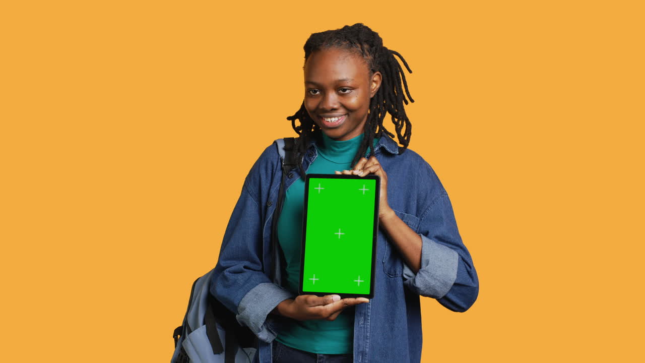 Smiling woman presenting tablet with green screen display, studio ...