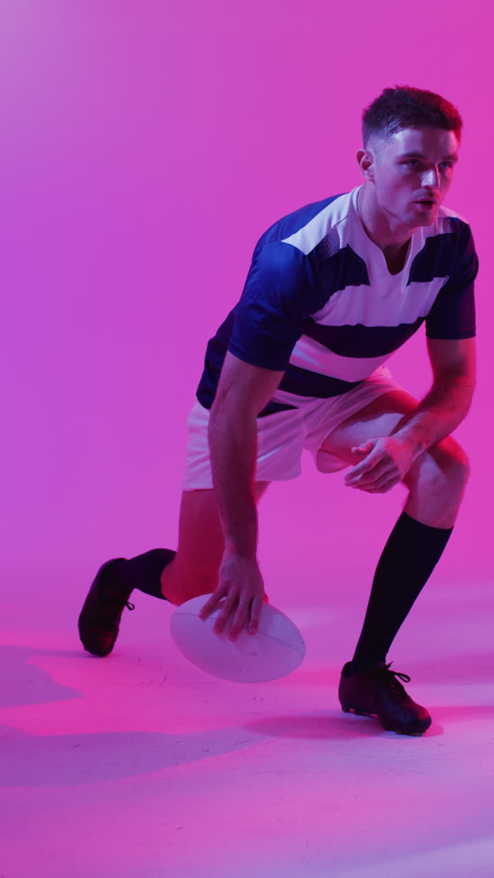Vertical video of caucasian male rugby player crouching with rugby ball ...