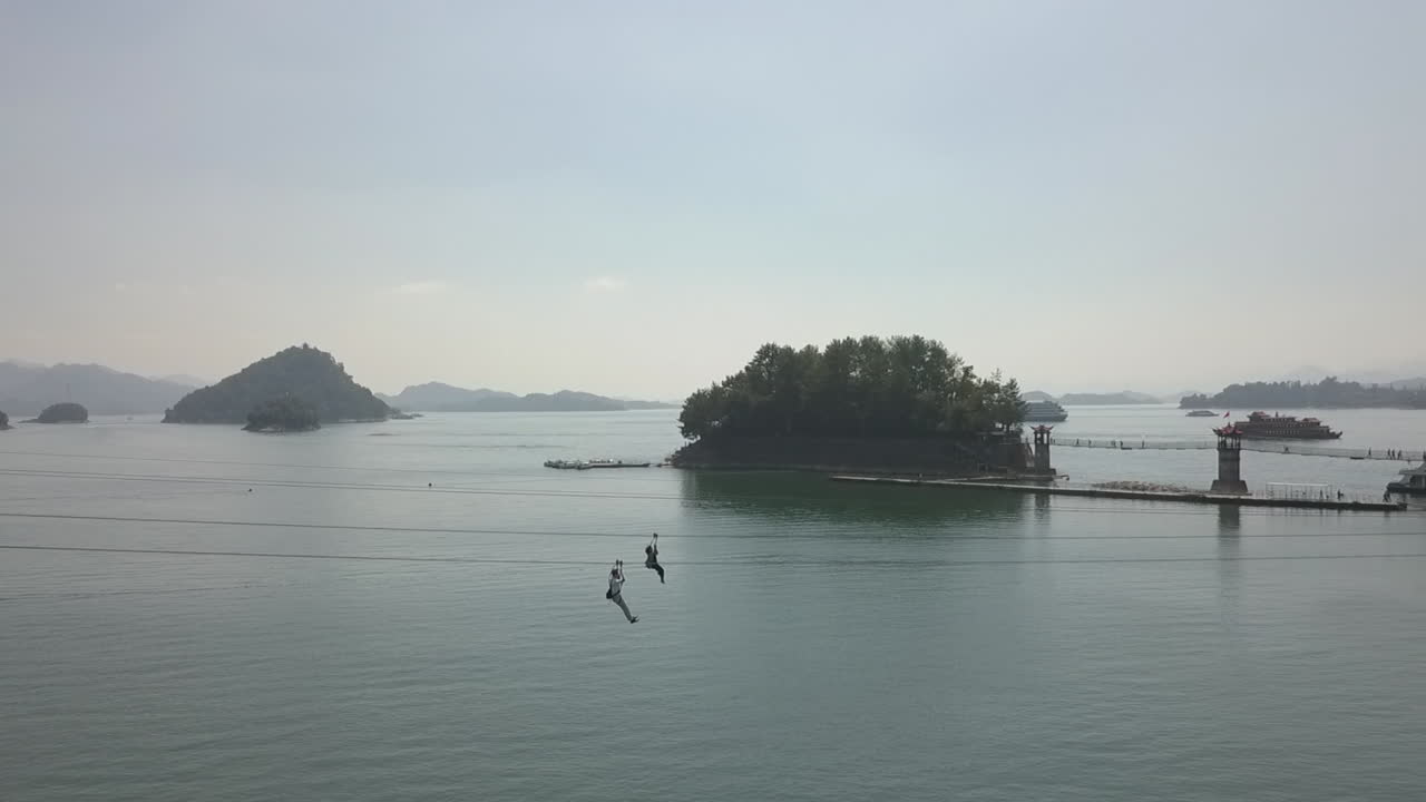 Aerial pan follows tourists sliding down zip line over lake in China ...