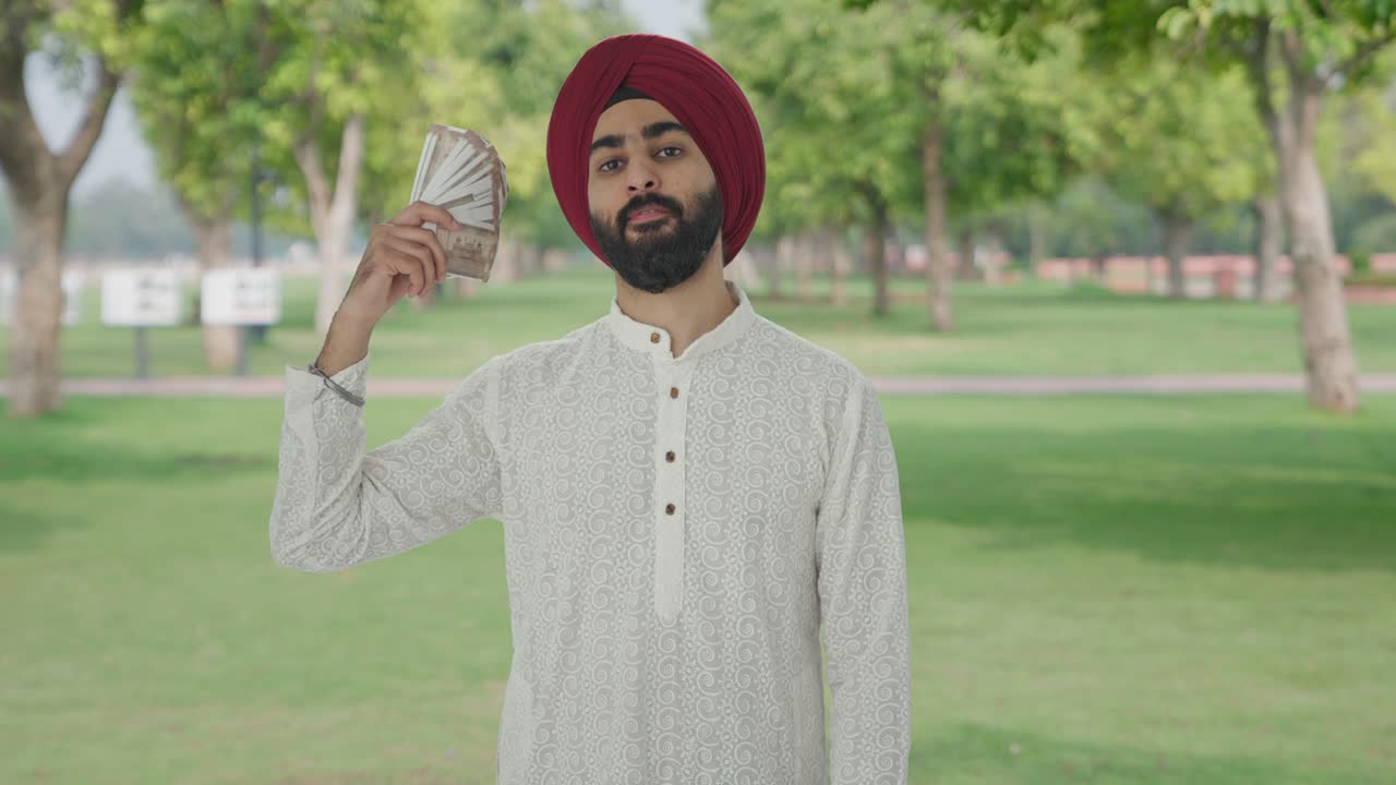 Premium stock video - Egoistic sikh indian man using money as fan in park