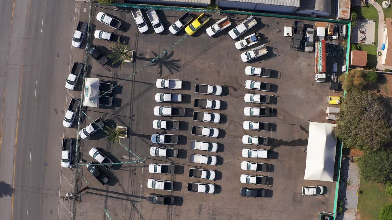 Aerial bird's eye descending spiral shot of trucks lined up at a used ...