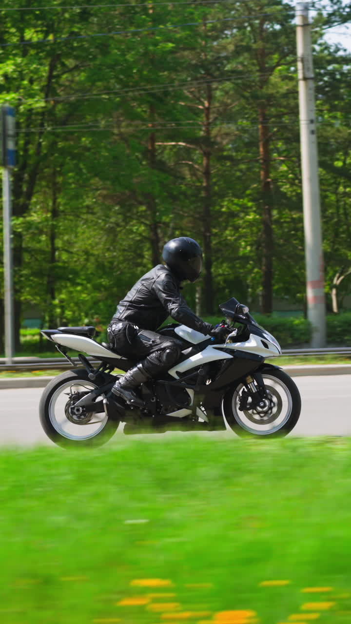 Biker in black uniform and hardhat rides powerful motorcycle along ...