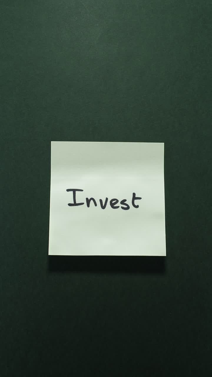 Hands posting Invest sticky note on dark green wall, representing ...