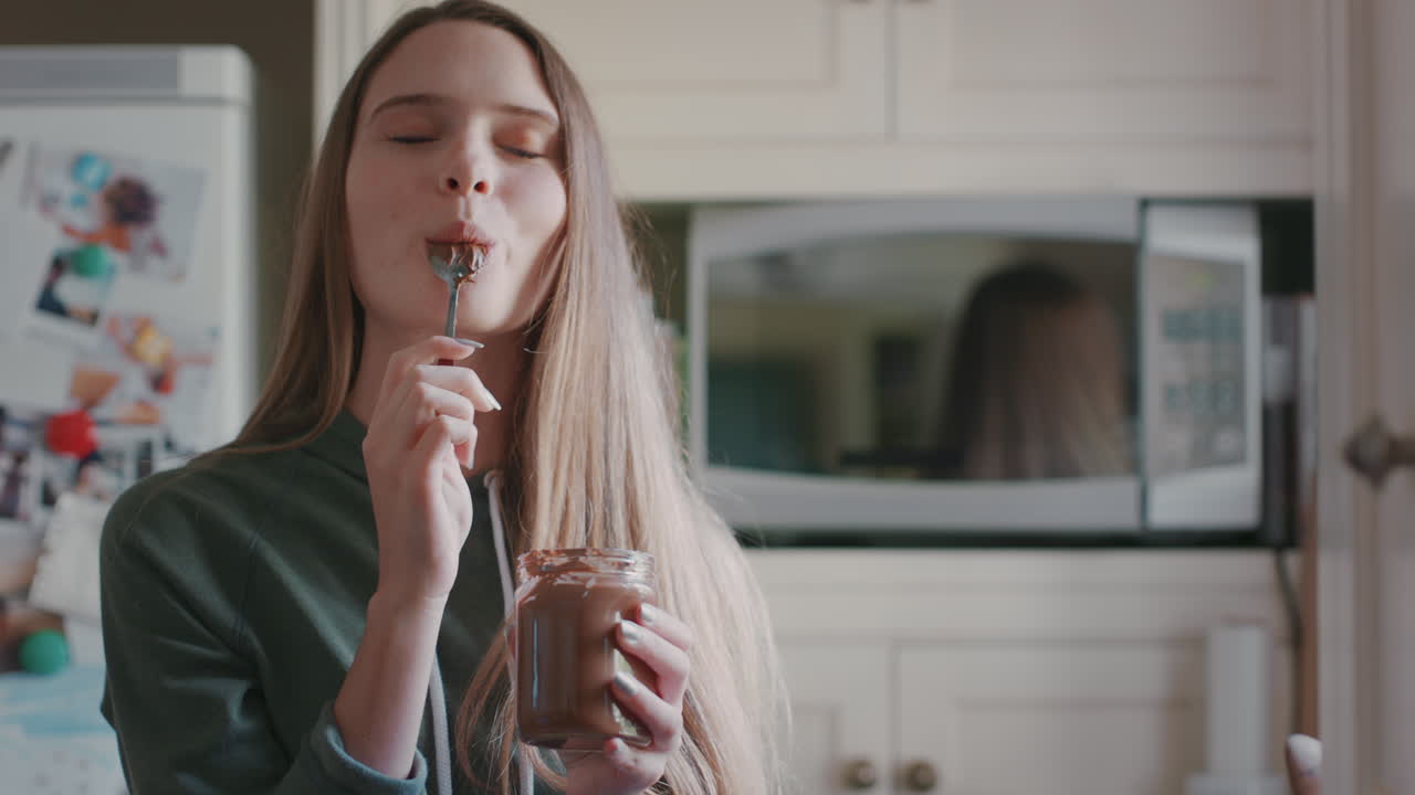 Sneaky teenage girl eating chocolate spread from jar in kitchen ...