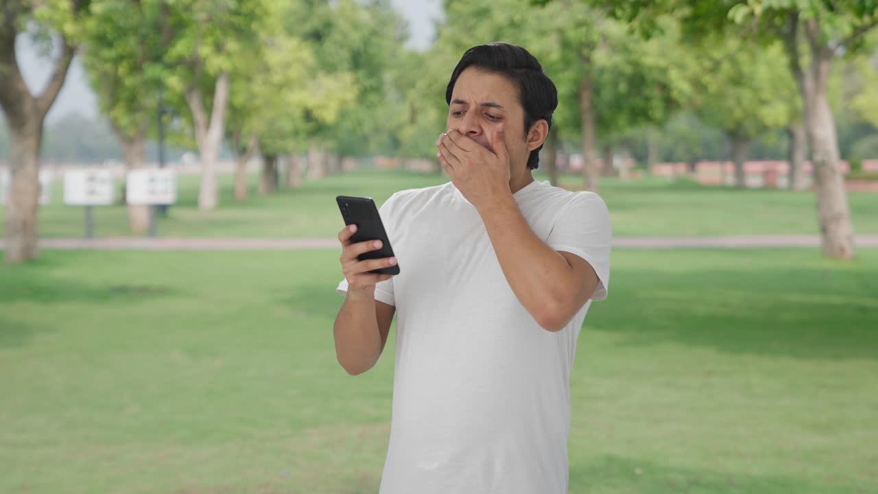 Premium stock video - Tired indian man scrolling through phone