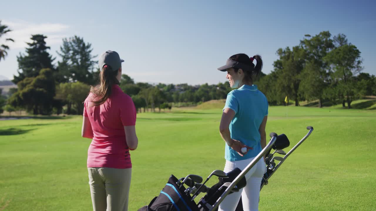 Two caucasian female golf players talking standing on golf field ...