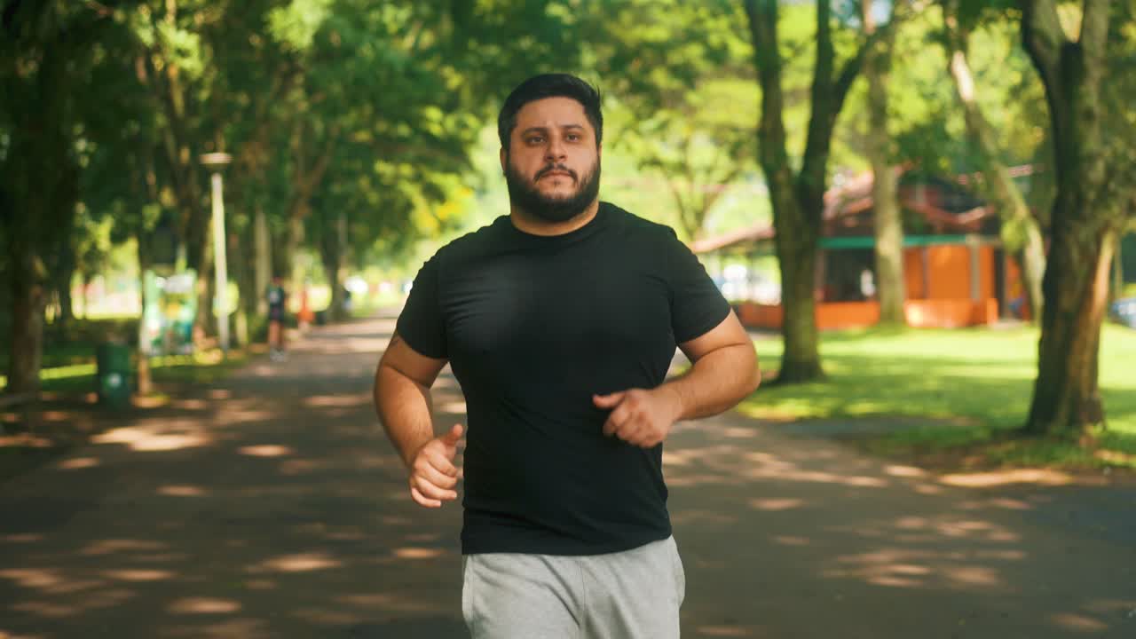 Front view following man jogging at the park on a sunny summer day slow ...