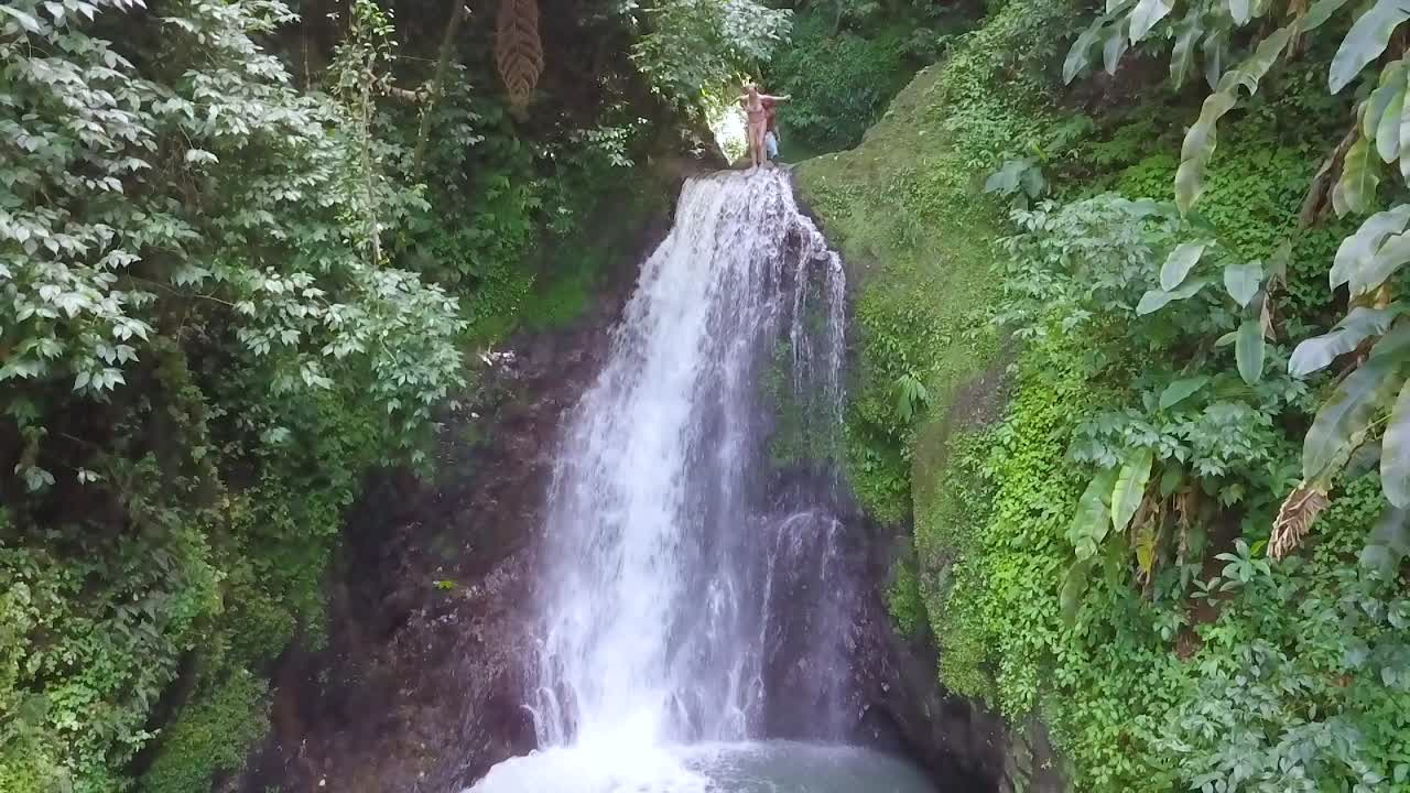 Slow motion woman diving from a waterfall into a pool in a tropical ...