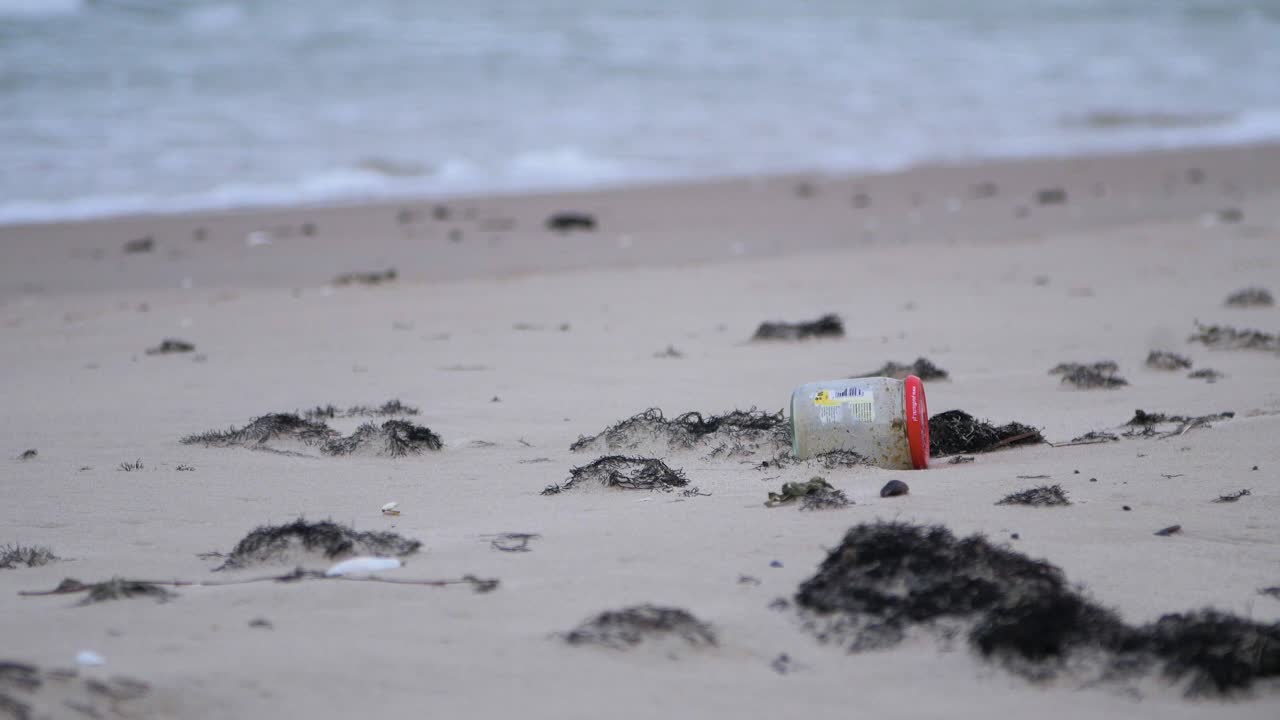 Glass jar on the beach with seaweed, trash and waste litter on an empty ...