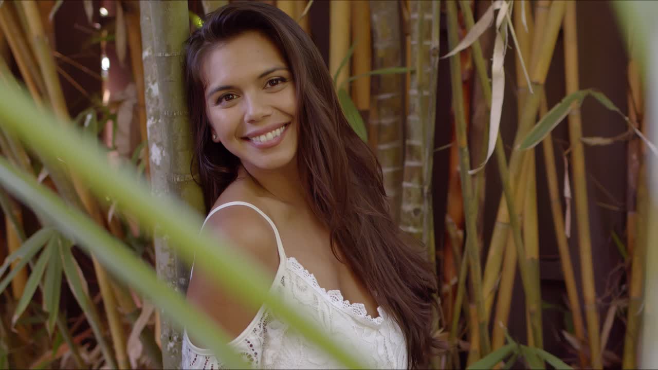 Pretty smiling woman leaning on bamboo tree Premium Stock Video Footage