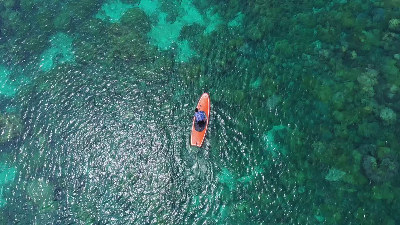 Bird's eye view of the man rowing on a paddle board at the clear ...