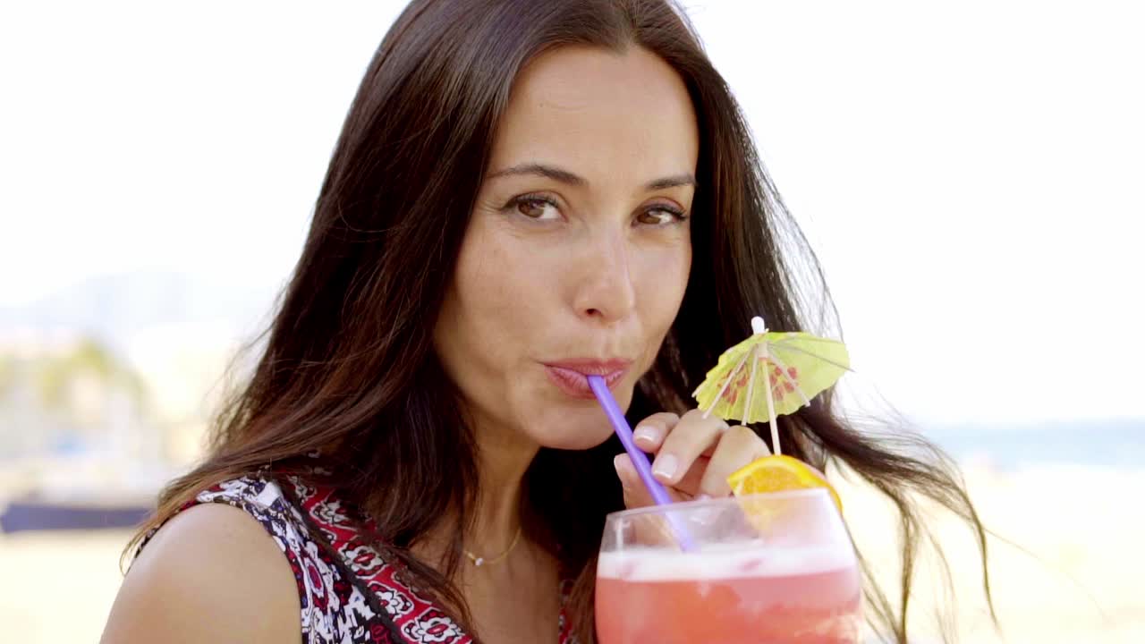 Premium stock video - Pretty woman sipping a cocktail at the beach