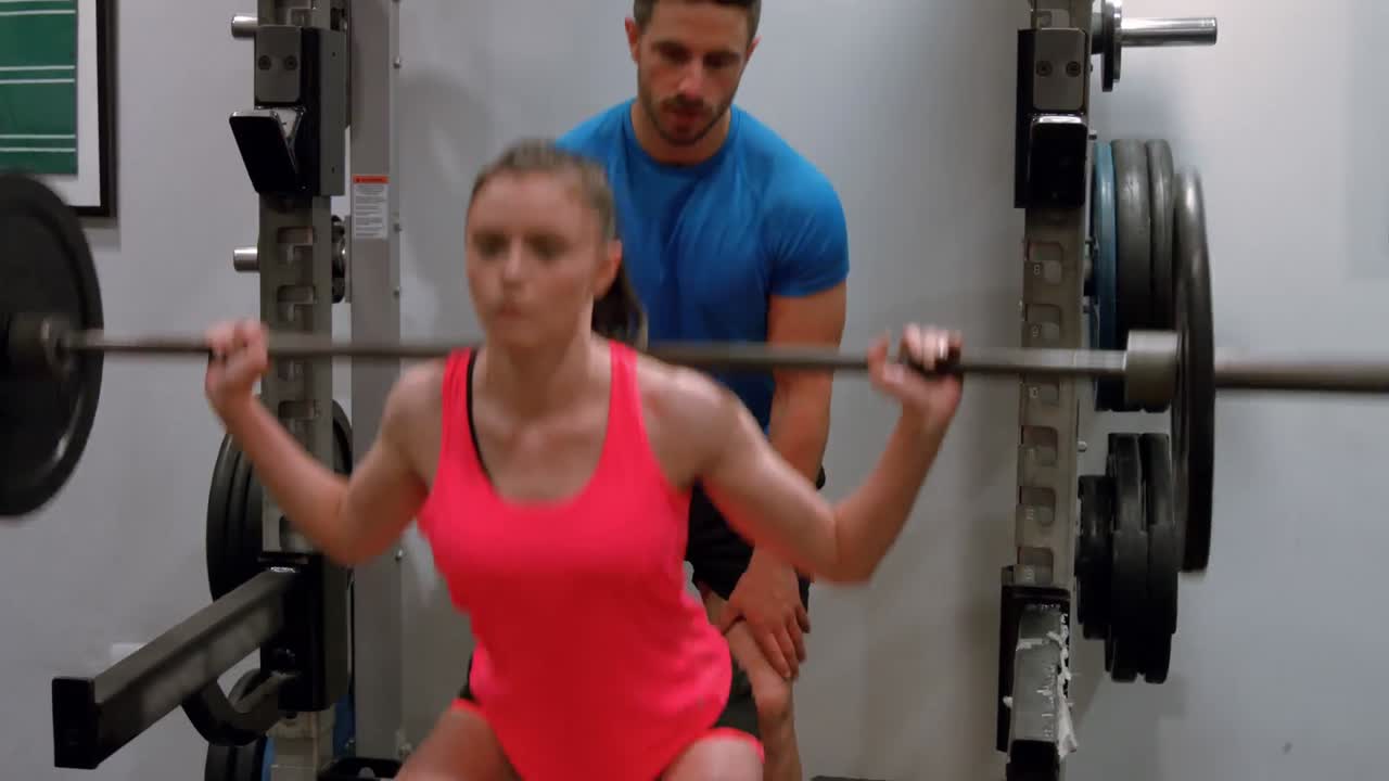 Premium stock video - Trainer spotting woman lifting weight