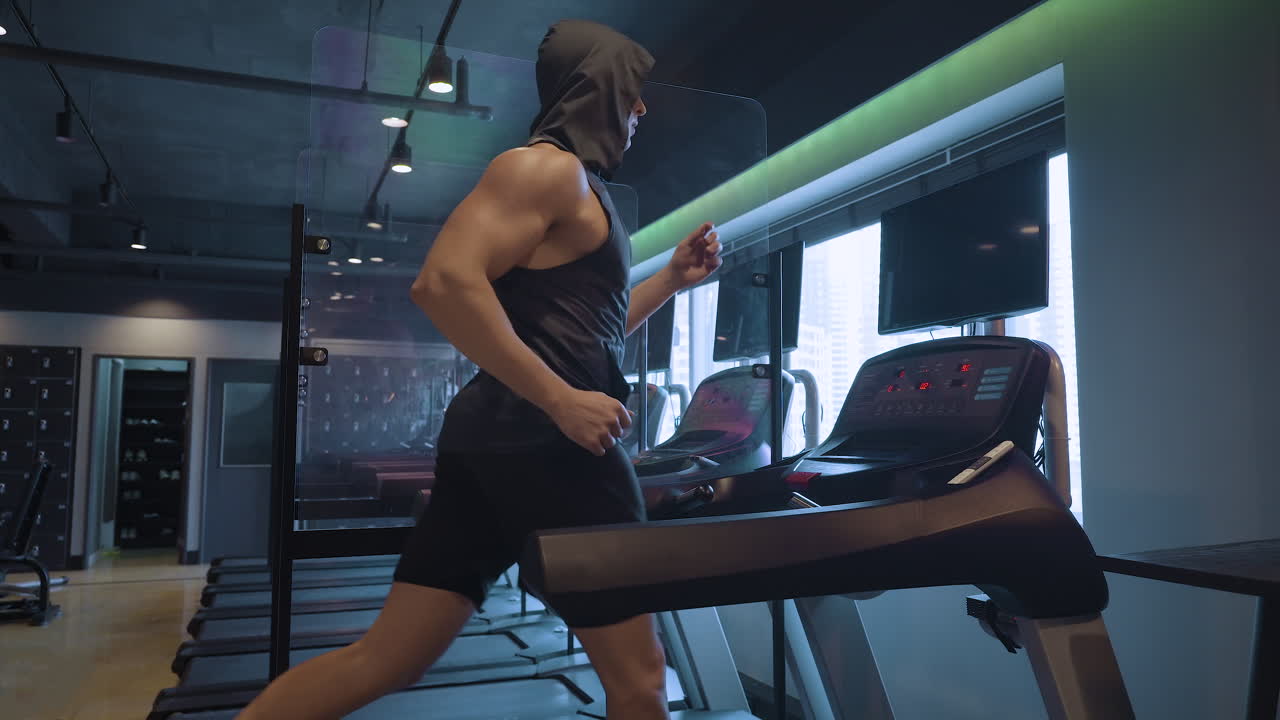 Fit muscular man runs in slow motion on treadmill inside empty gym ...