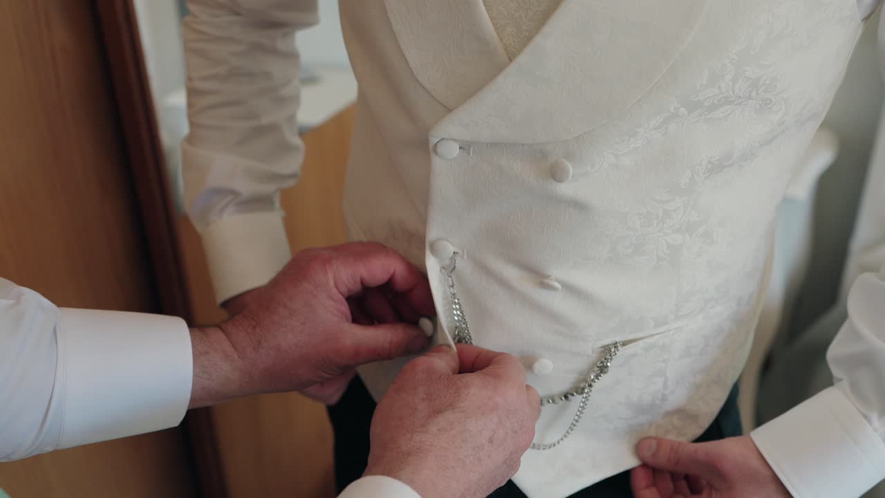 Close up of man fastening ornate white vest with chain detail indoors ...