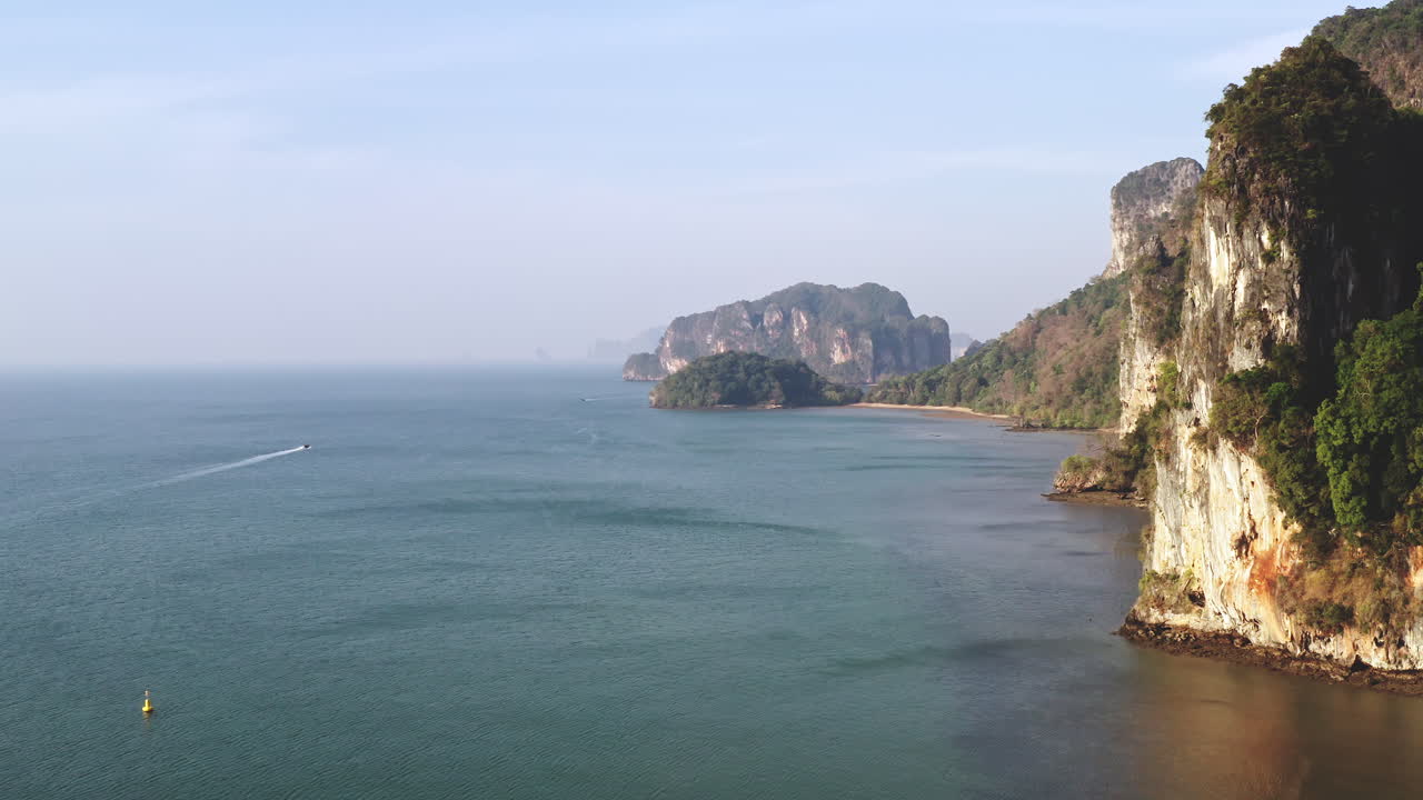 Massive coastal limestone cliffs in Andaman sea, boat cruising below ...