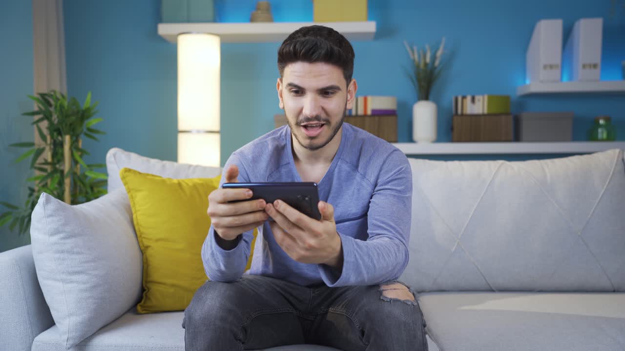 Premium stock video - Man watching video on smartphone alone at home.