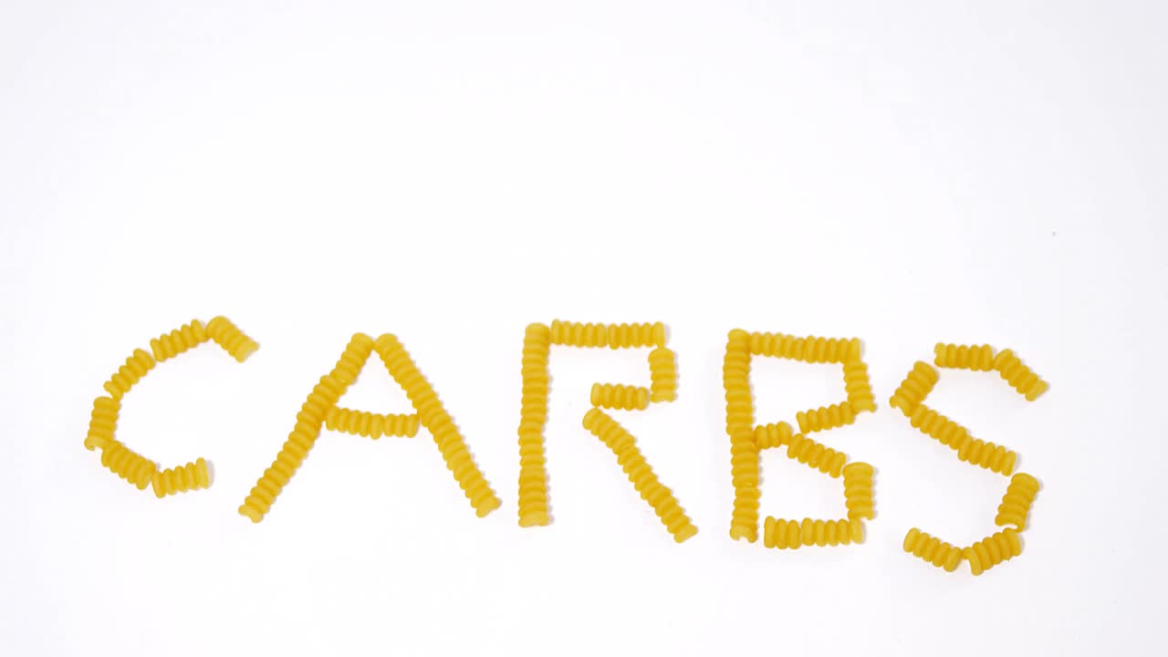 Premium stock video - Text carbs written with pasta on white background