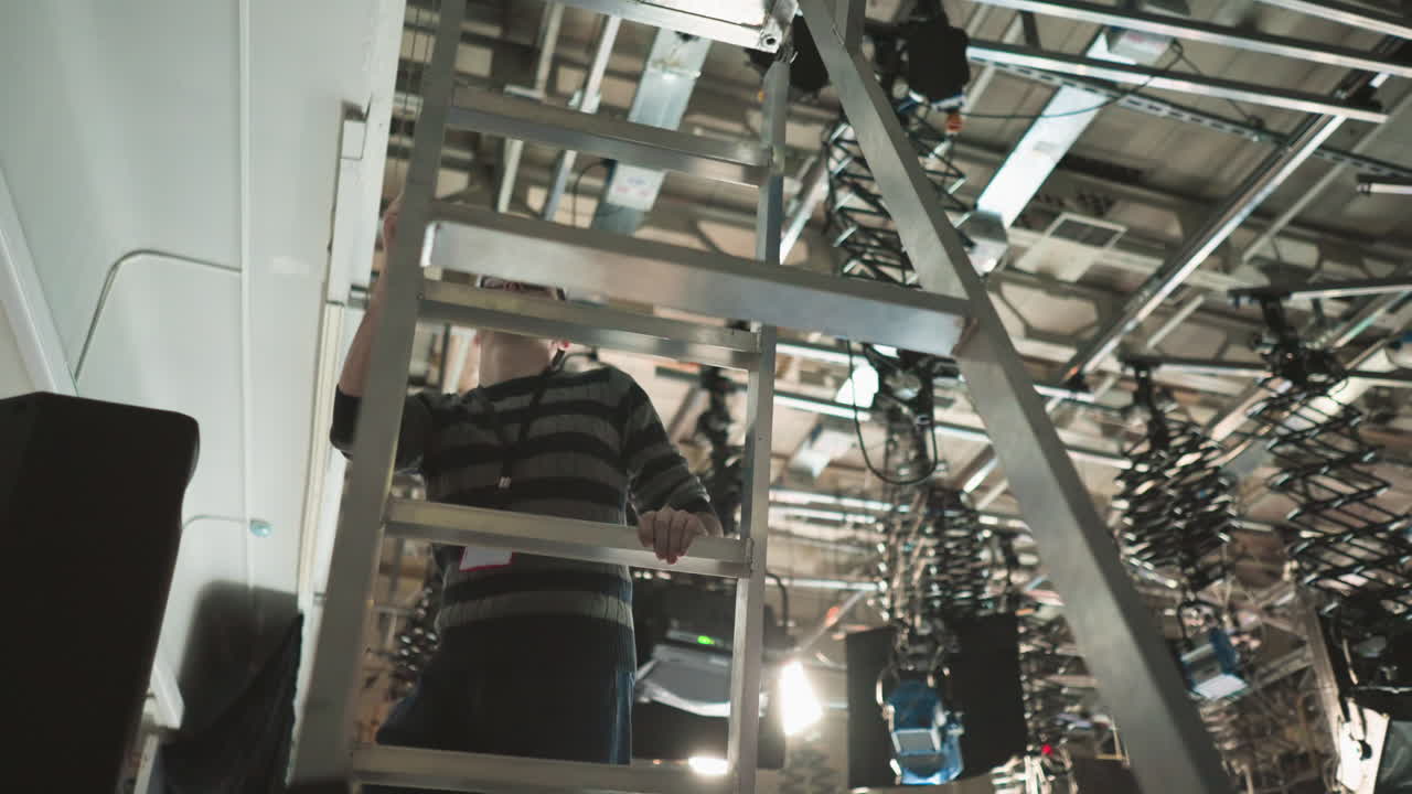 Studio technician climbing ladder for equipment adjustment, managing ...