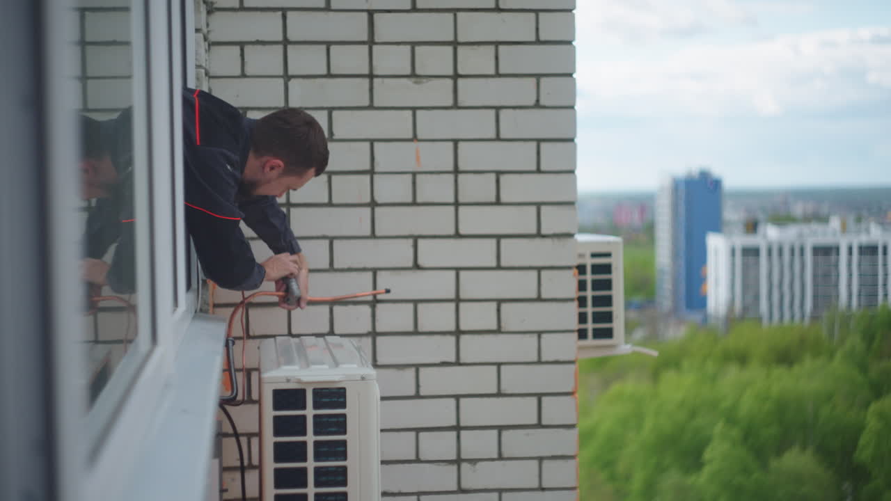 Premium stock video - A man at high altitude installs air conditioning ...