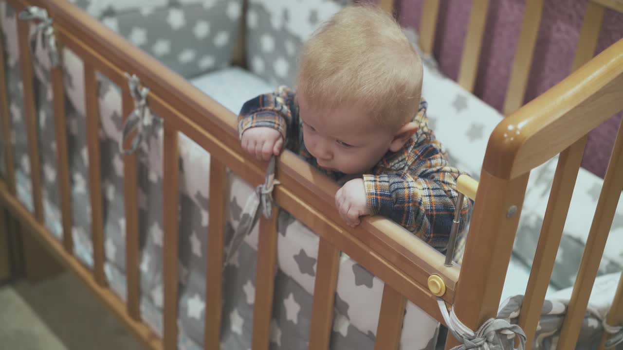 Premium stock video - Little baby leans on wooden cot with soft linen ...