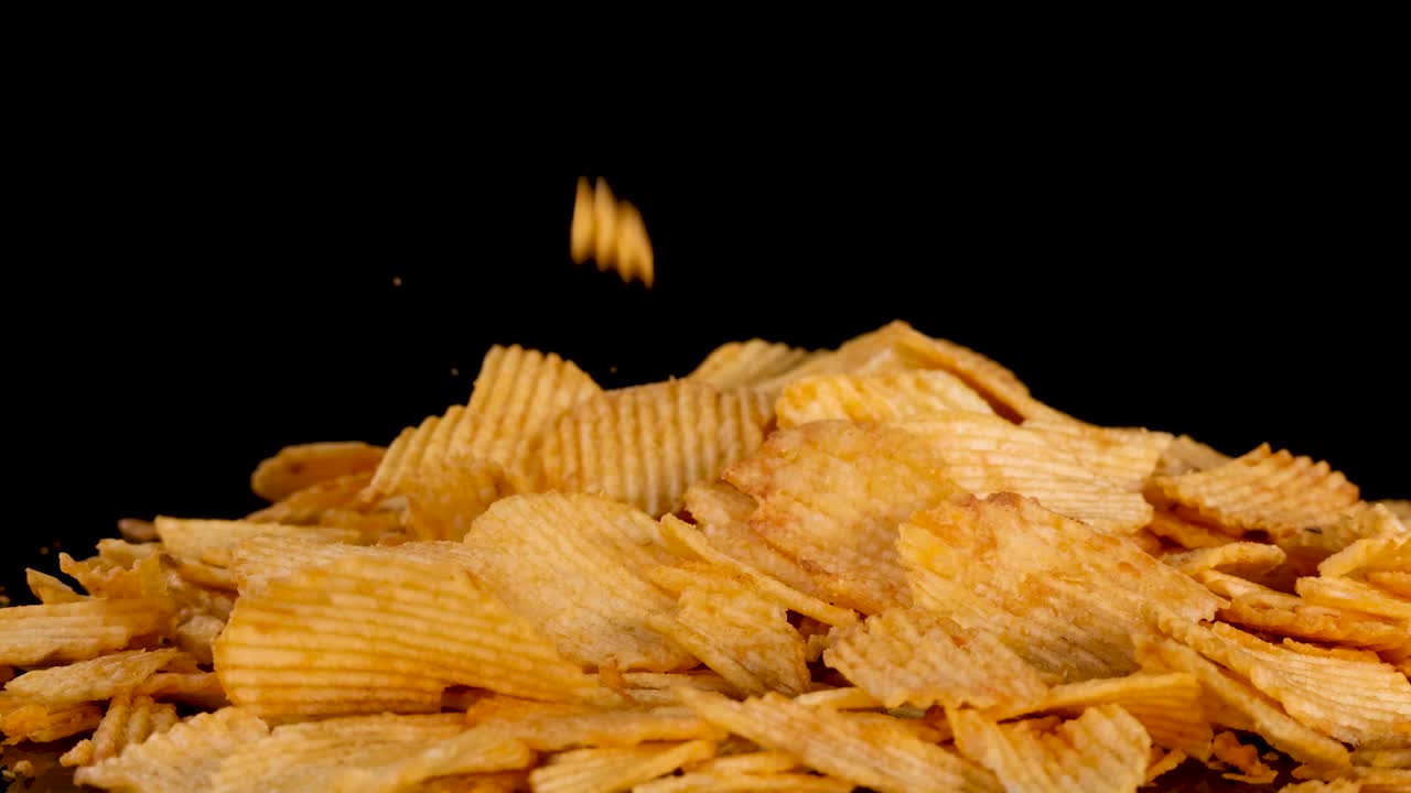 Ridged potato chips fall onto a pile in slow motion, captured in close ...
