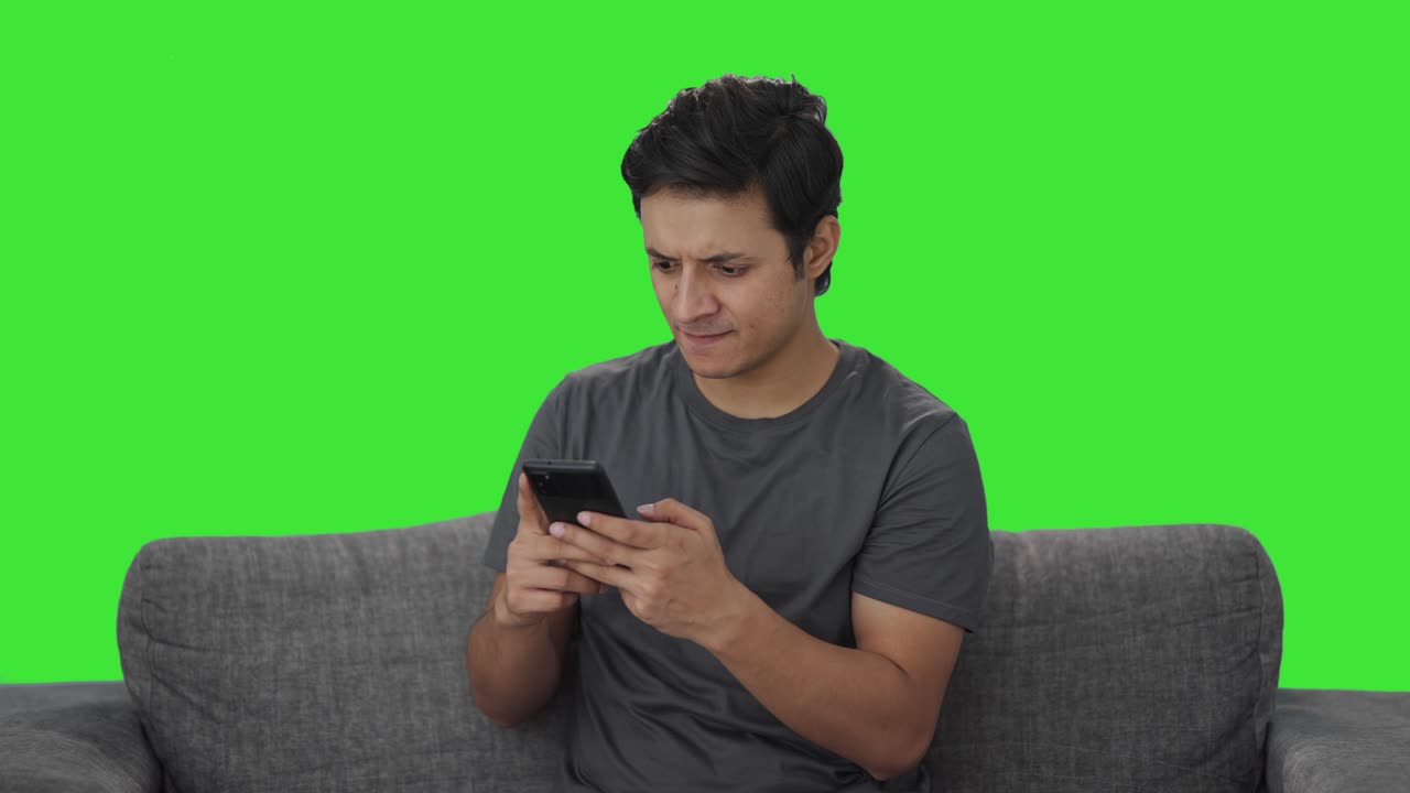 Premium stock video - Frustrated indian man typing on phone green screen