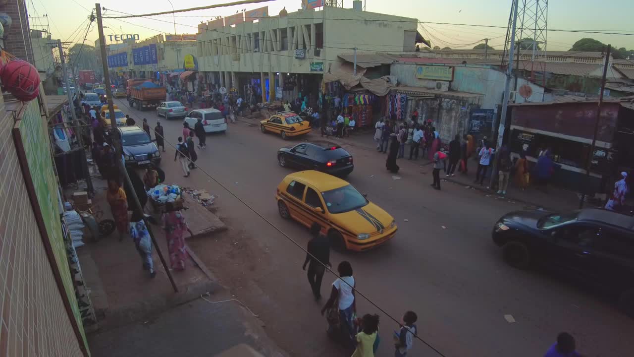 Bustling Serekunda Market street with pedestrians and cars at sunset ...