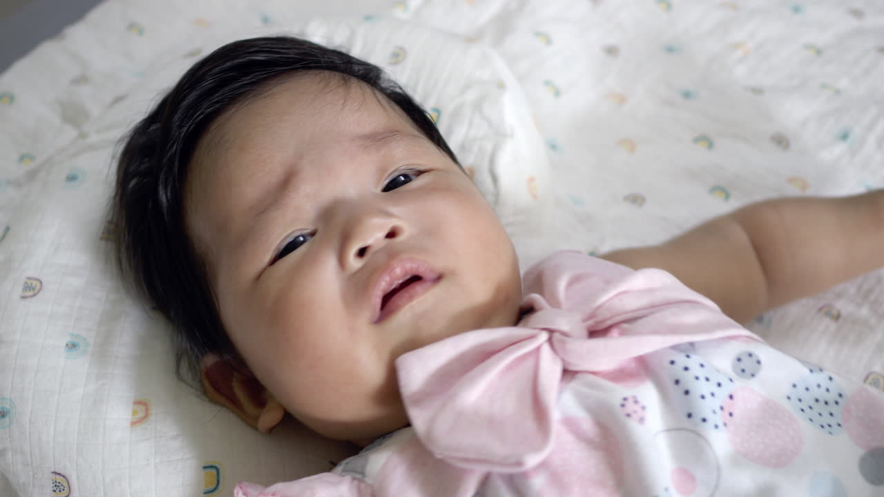 Close-up of an adorable baby girl in a pink bow, expressing discomfort ...