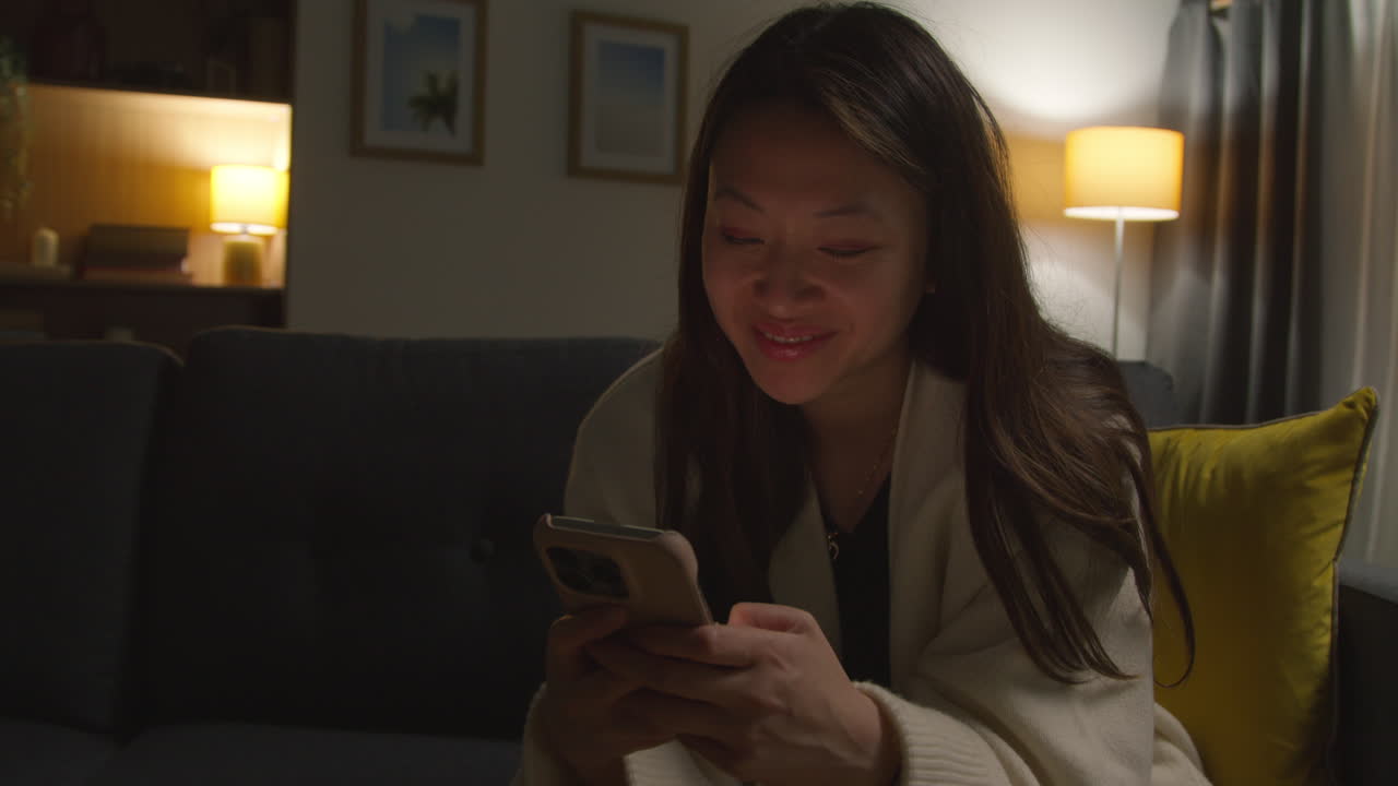 Vídeo Gratis - Mujer que pasa la noche en casa sentada en el sofá con el teléfono móvil ...