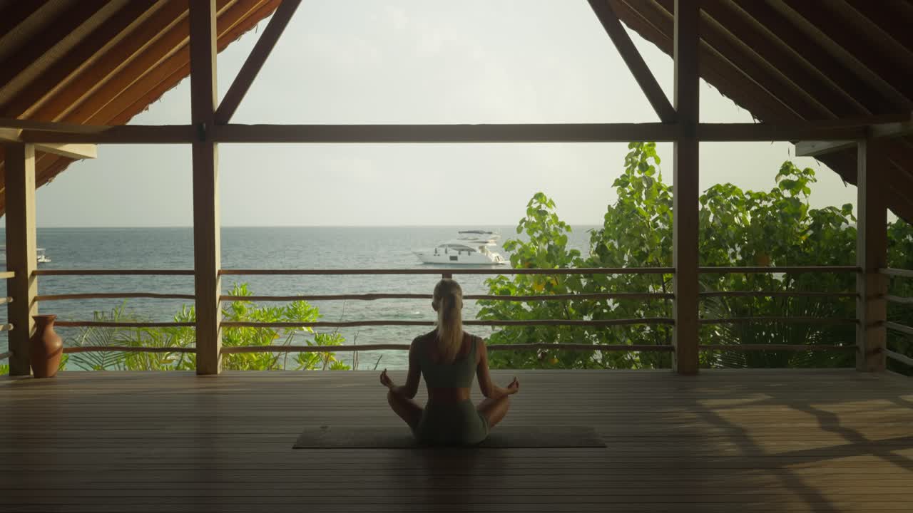 Woman sitting in yoga easy pose meditating to soothing ocean sound in ...