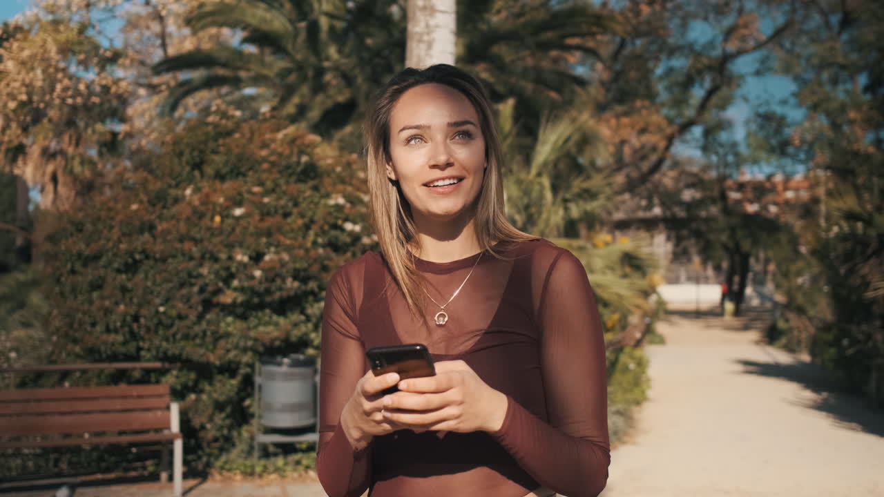 Free stock video - Young woman happily texting on the phone in the street.