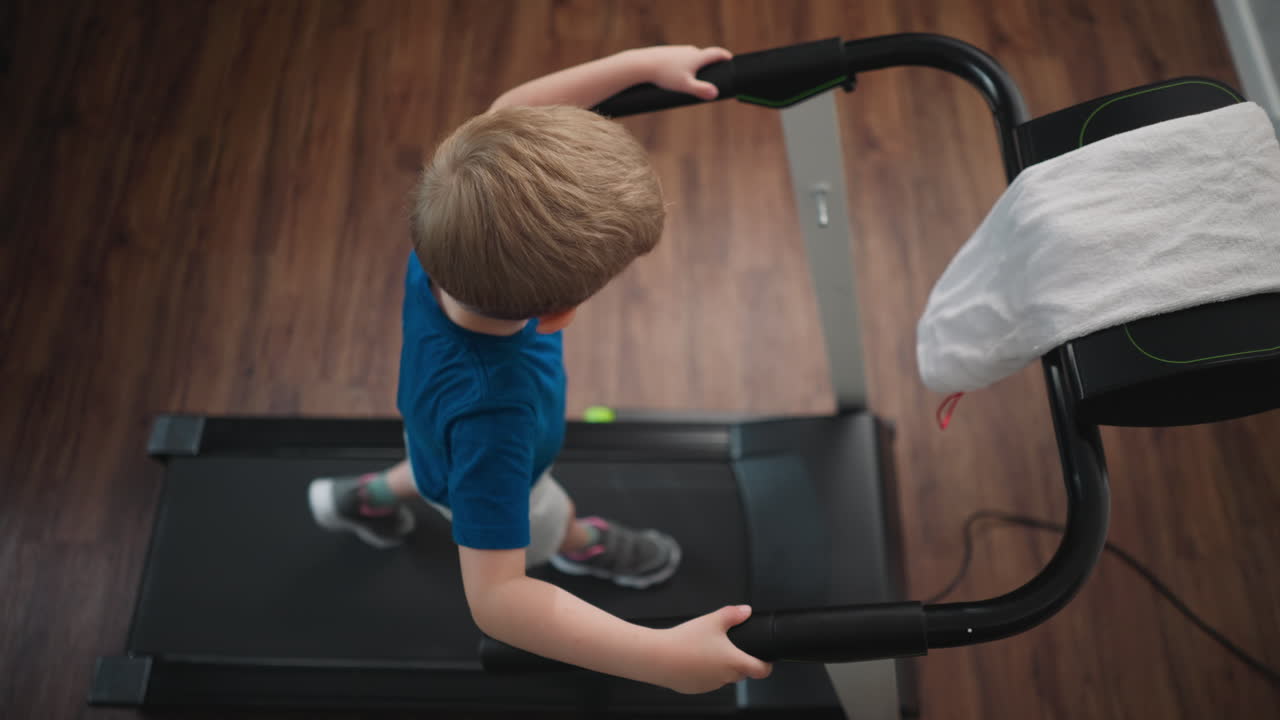 Overhead shot of young kid walking on treadmill, gripping both handles ...