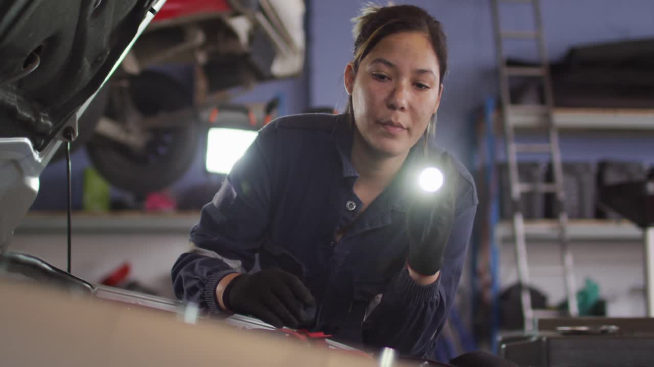 Female mechanic using a torch light and repairing a car at a car ...