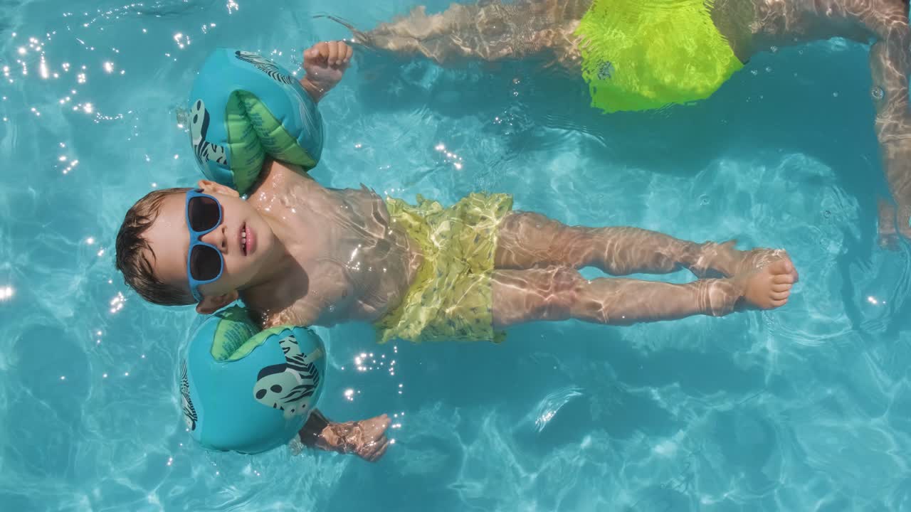 Relaxed small boy wearing sunglasses floating on swimming pool using ...