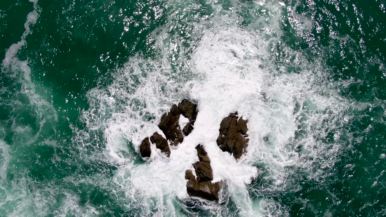 Rough ocean waves crashing against sharp rocks - aerial overhead view ...