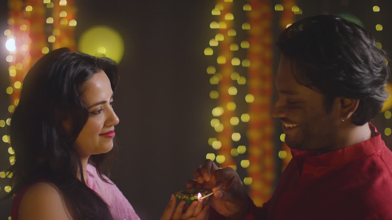Side view of young couple celebrating festival of diwali lighting diya ...