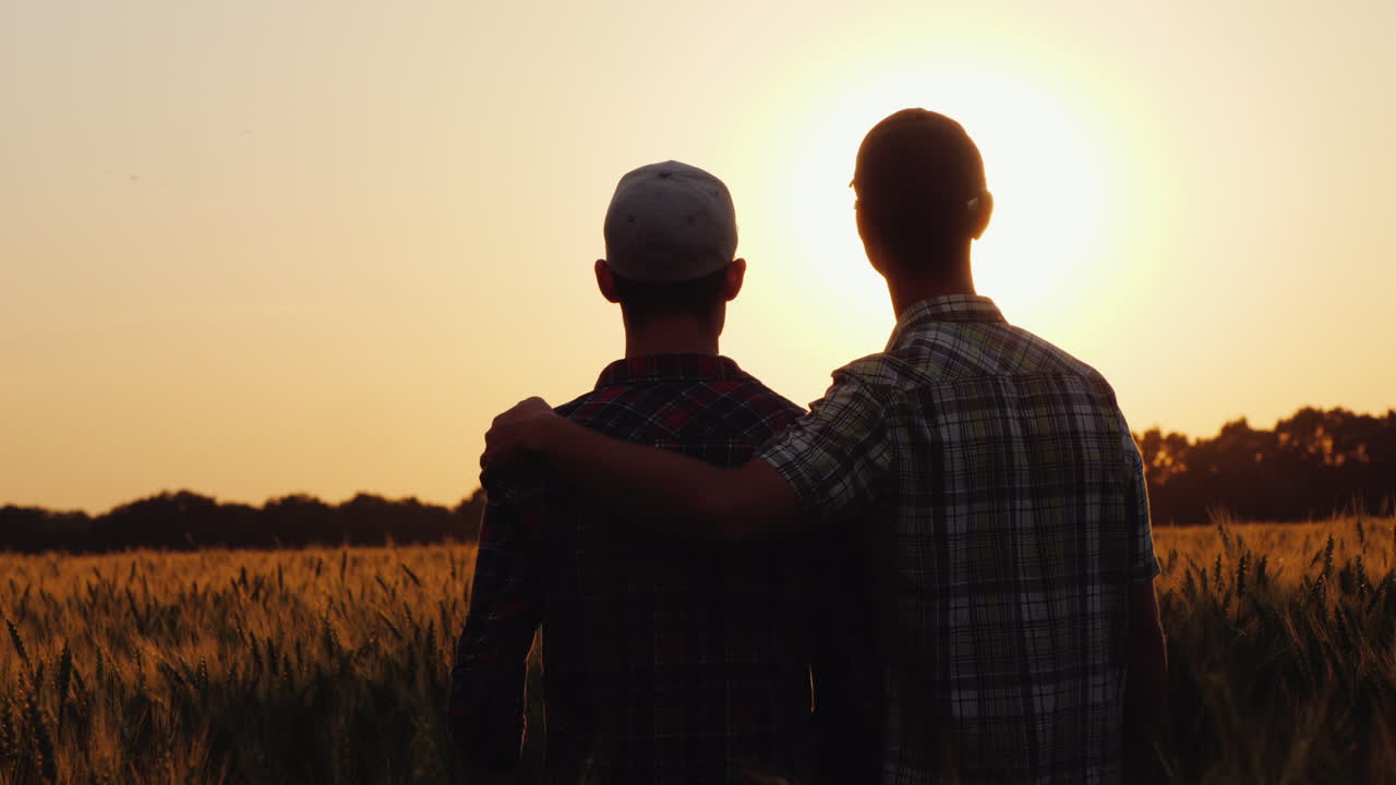 Premium stock video - Two men gently hug while looking at a wheat field