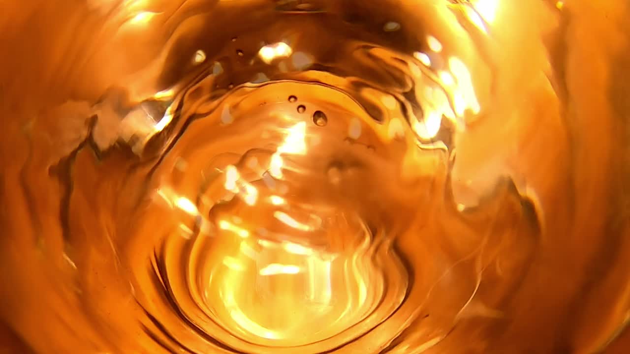 Premium stock video - Golden effect of water drops falling into full glass