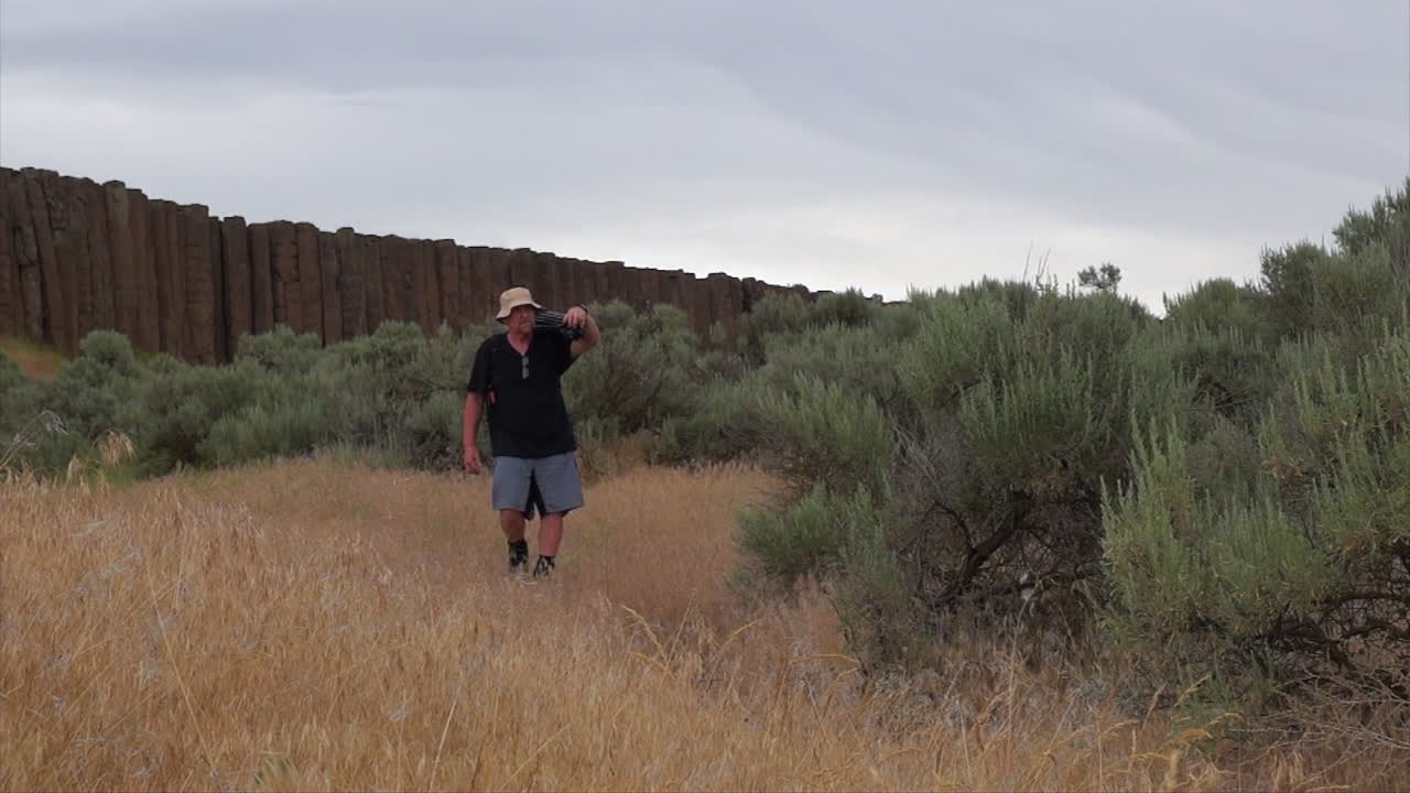 Male photographer carries large camera and tripod in western sagebrush ...