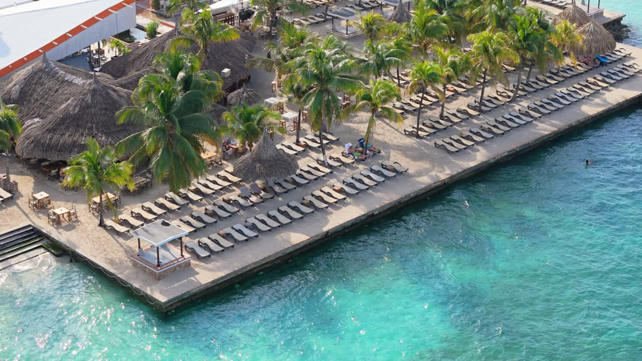 Drone orbit around tropical lounge chairs in shade of palm trees at ...