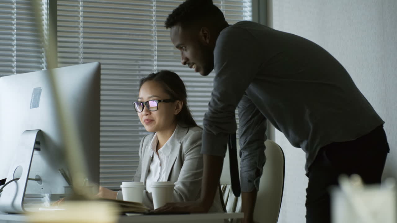 Black man in glasses and woman sitting at office desk and viewing ...