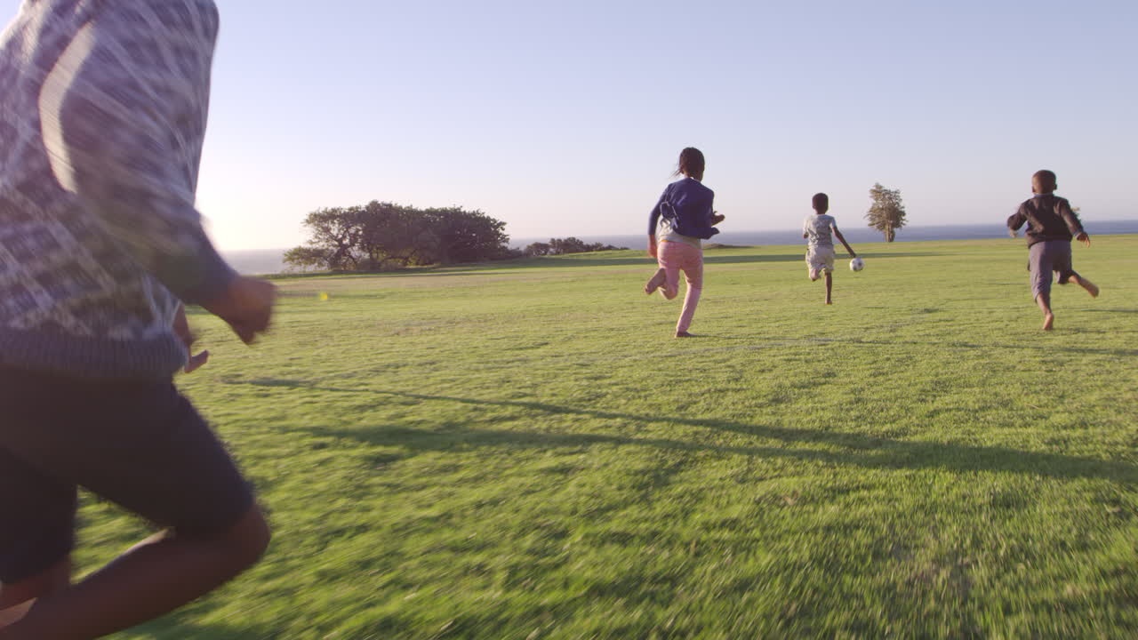 Premium stock video - Elementary school kids chasing football in a field